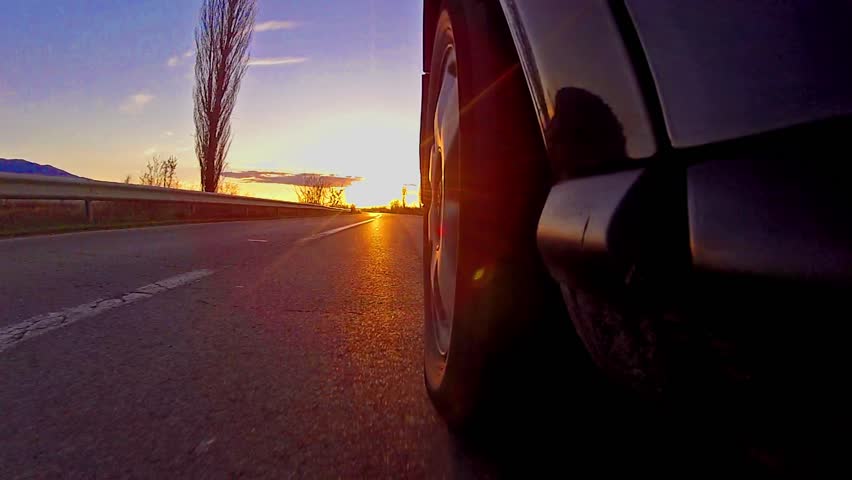 Sport Car Driving Down Narrow Road Toward Sun Rays At Sunset, Low Angle ...