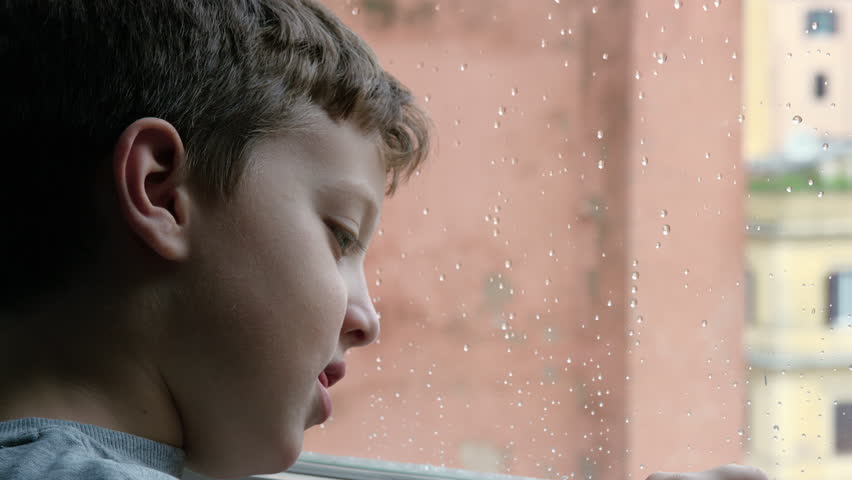 Sad Child Looks At Raindrops Through Window Glass Alone In An Apartment ...